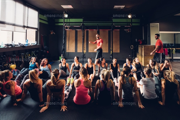 Large group of women training in gym with male trainers, sitting on ...